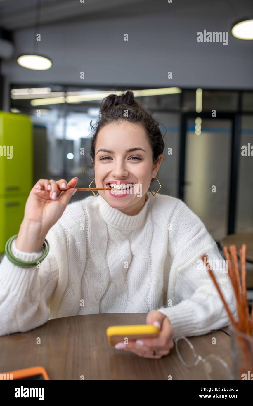 Young woman chewing bread sticks, holding mobile phone Stock Photo - Alamy