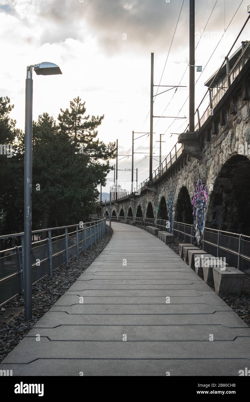 Long paved path beside the arches of a viaduct under a cloudy sky Stock ...