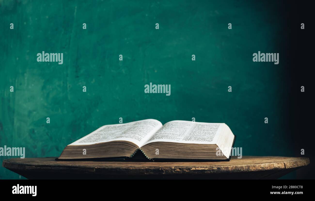 Open Holy Bible on a old round wooden table. Beautiful green wall ...