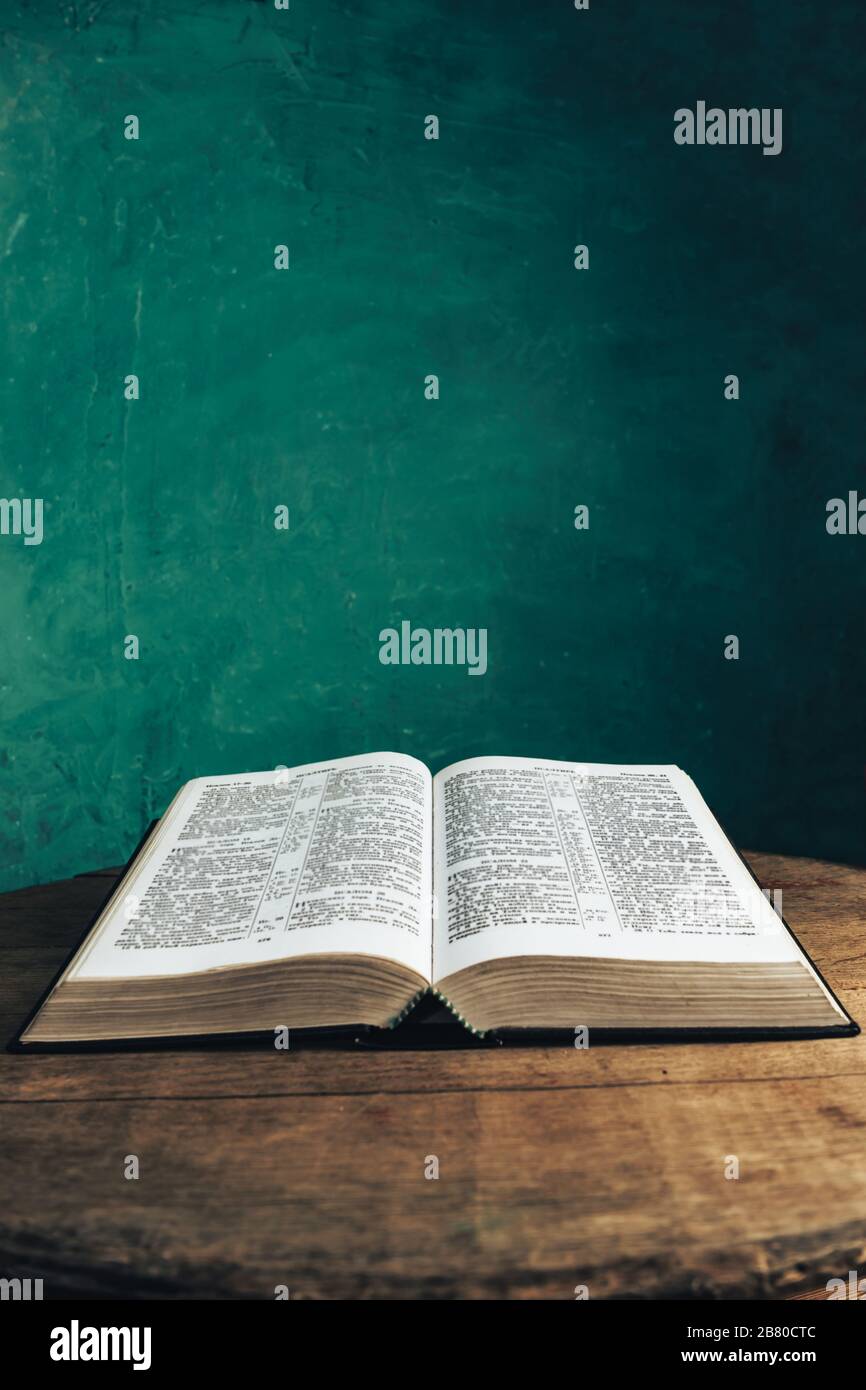 Open Holy Bible on a old round wooden table. Beautiful green wall ...