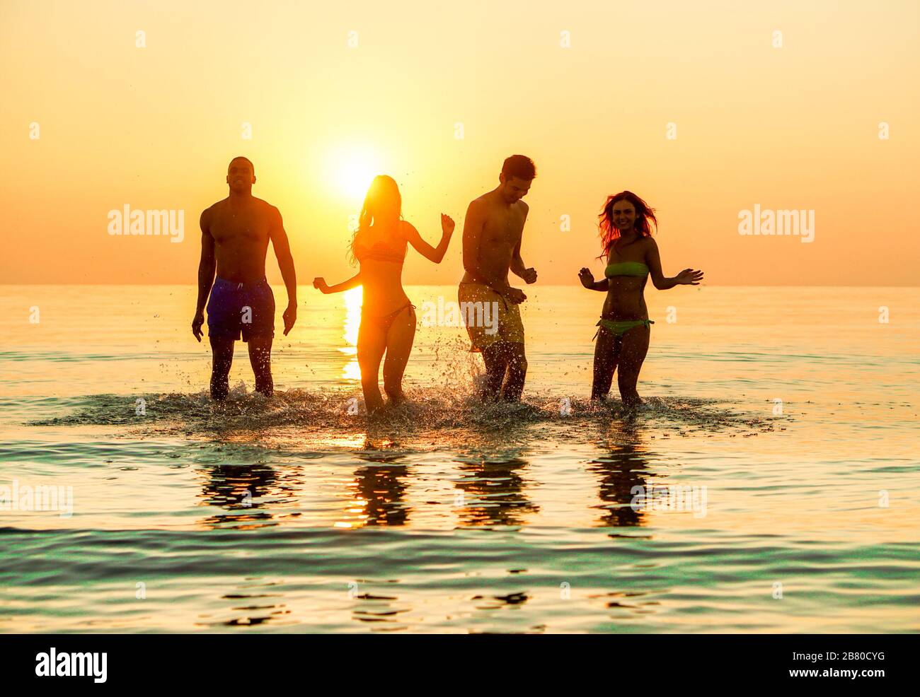 Silhouettes of young people swimming and jumping in ocean at sunset ...