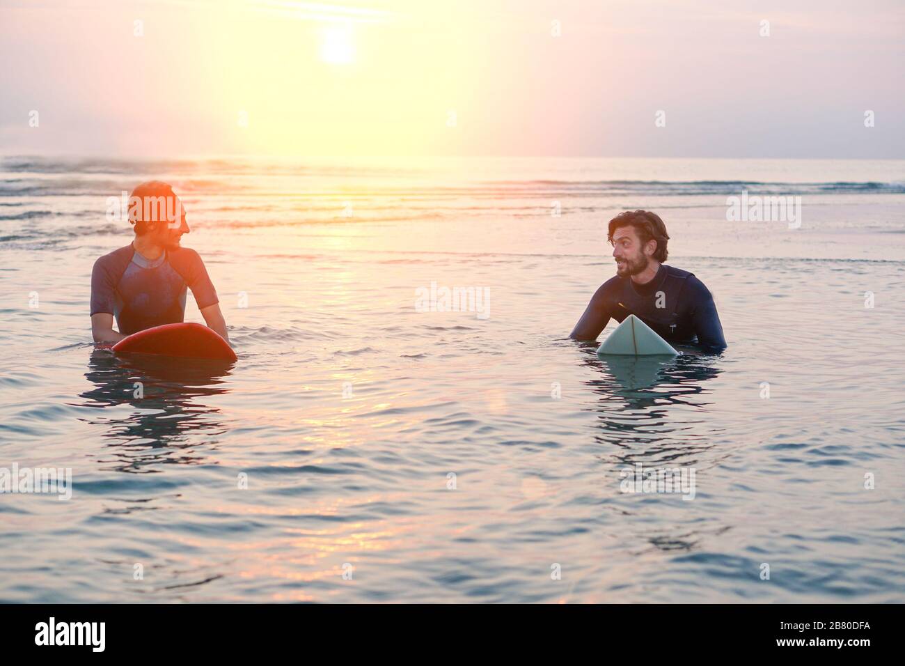 Two men in wetsuits with a surfboard on a sunny day inside water ...