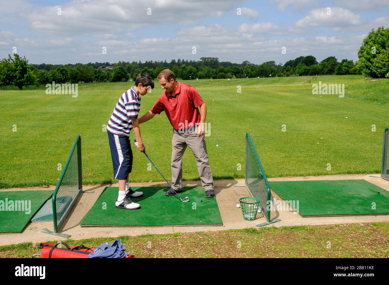 An adult golf instructor teaching a young teenage boy golfer the ...