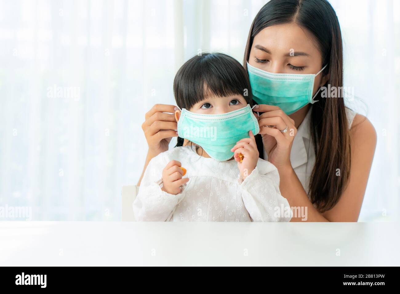 Asian mother wearing wearing to her daughter healthy face mask sitting ...