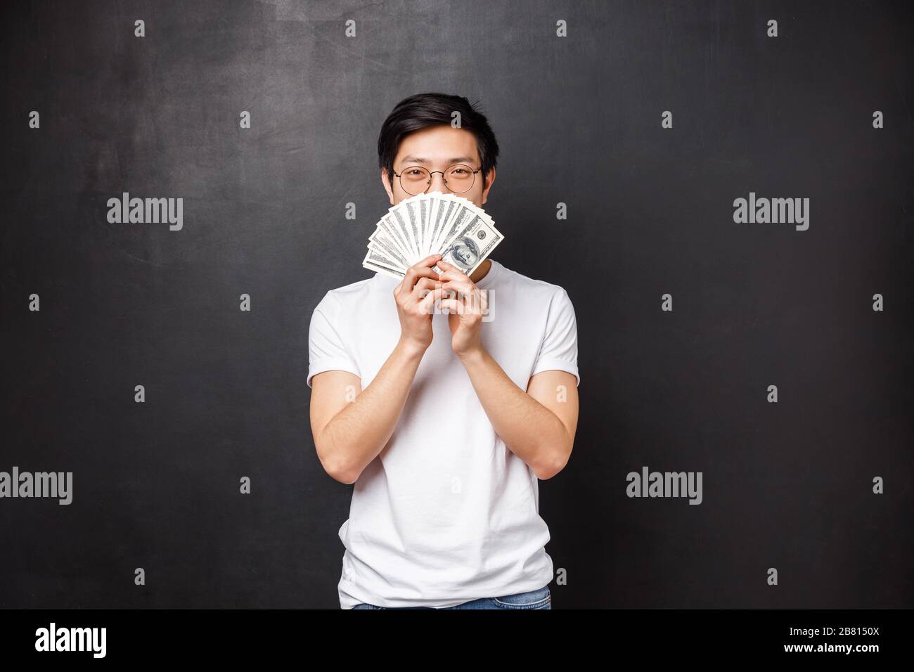 Portrait of sly happy and pleased asian young man winning big cash ...