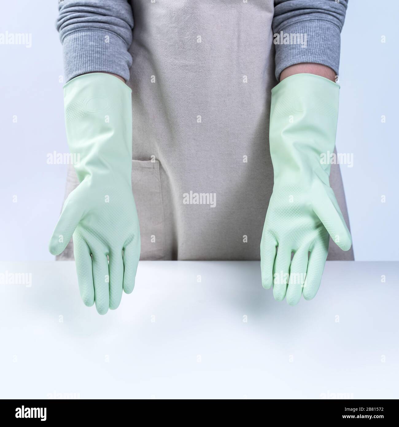 Young woman housekeeper in apron is wearing green gloves to clean the ...