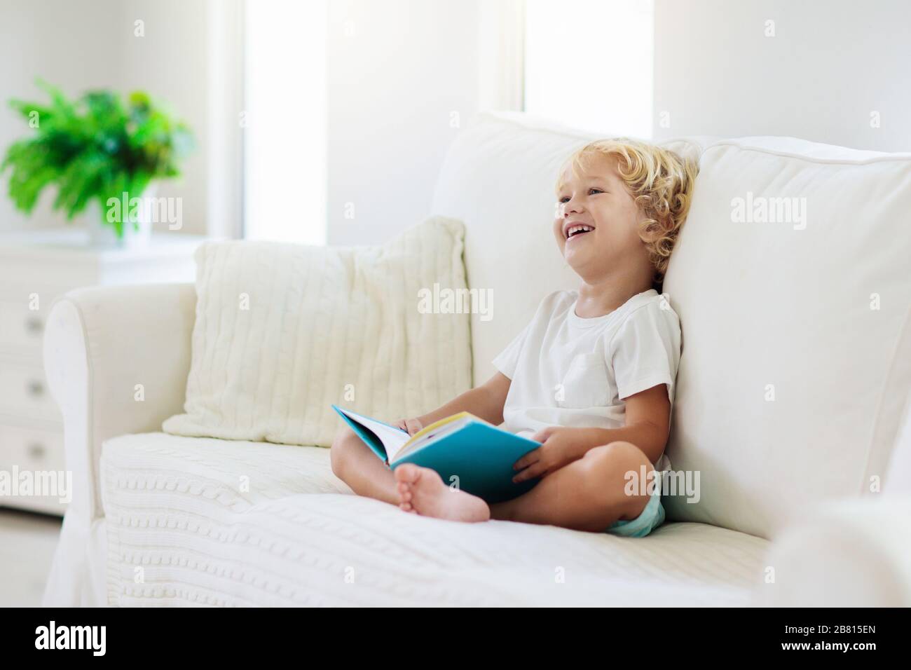 Child reading book. Kids read books. Little boy sitting on white couch ...