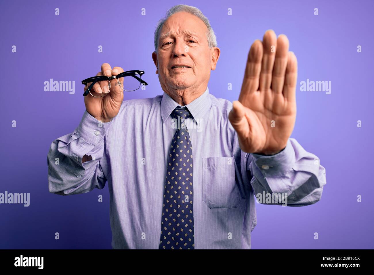 Senior grey haired man holding correction glasses over purple ...