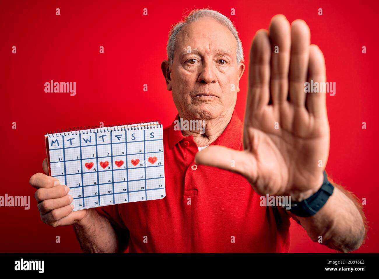 Senior grey haired man holding special date calendar over red ...