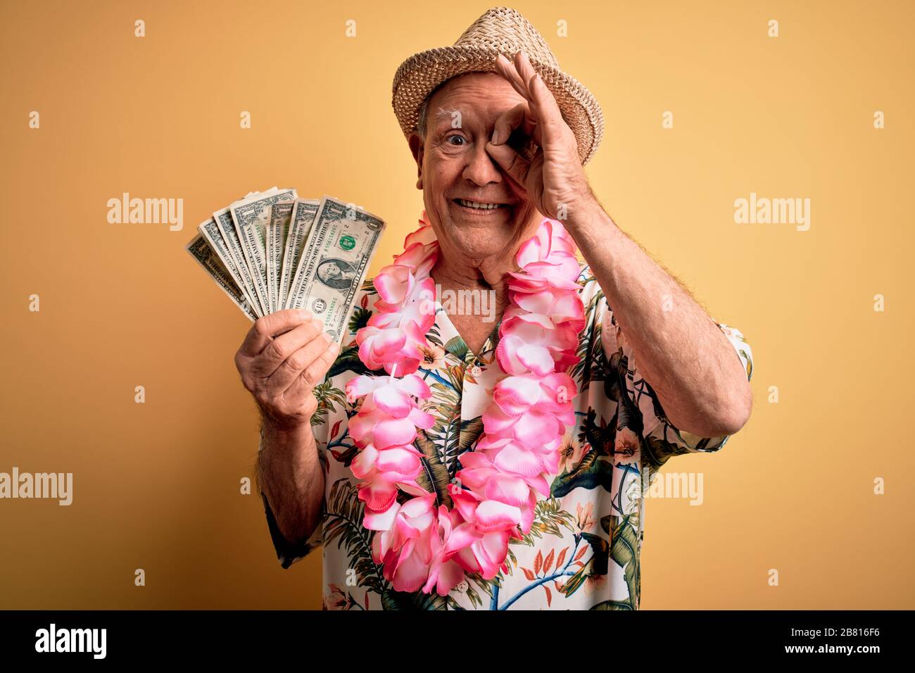 Grey haired senior man wearing summer hat and hawaiian lei holding ...
