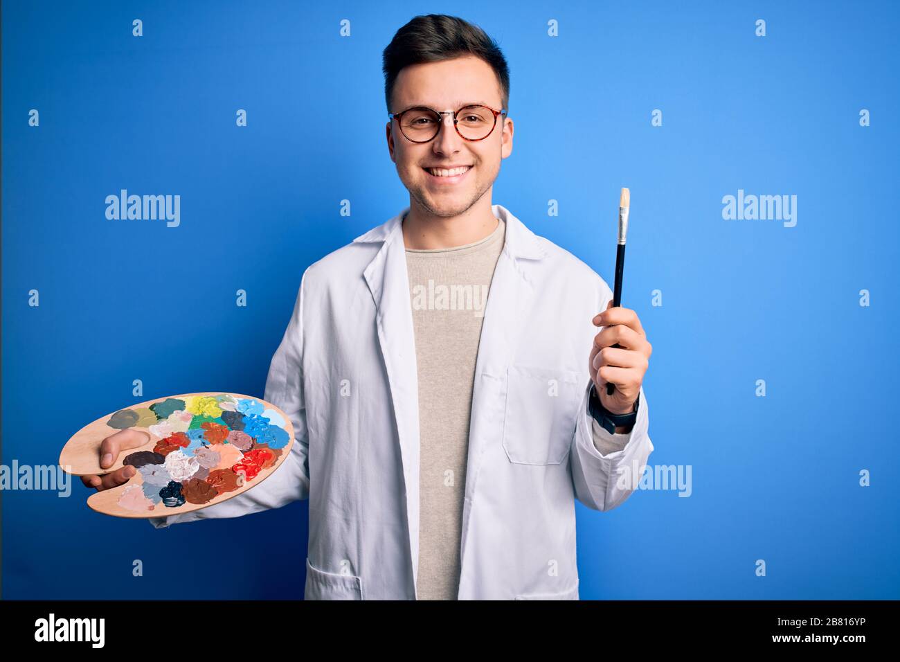 Young handsome caucasian artist man holding paintbrush and painter ...