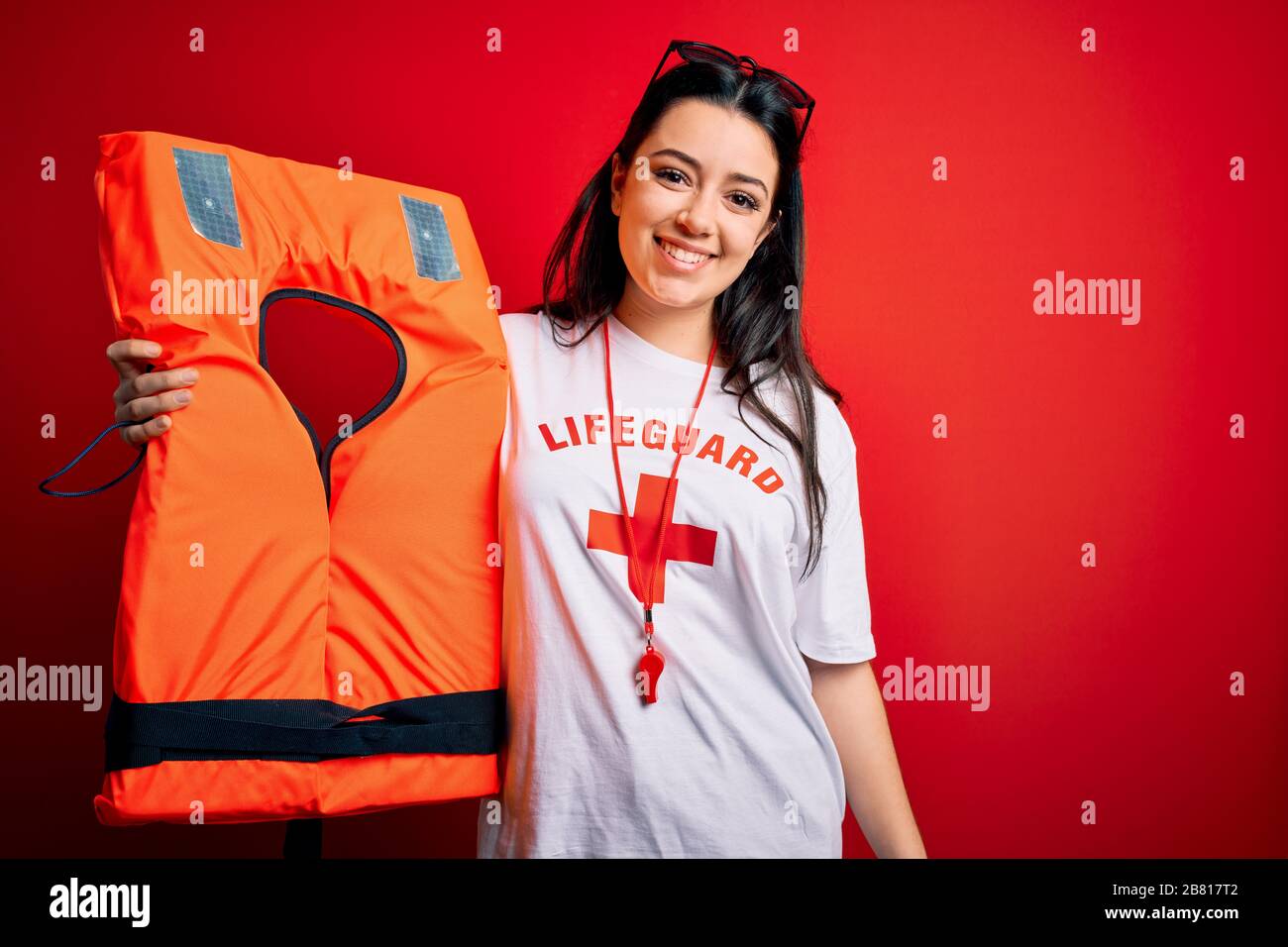 Young lifeguard woman holding rescue lifejacket over red background ...
