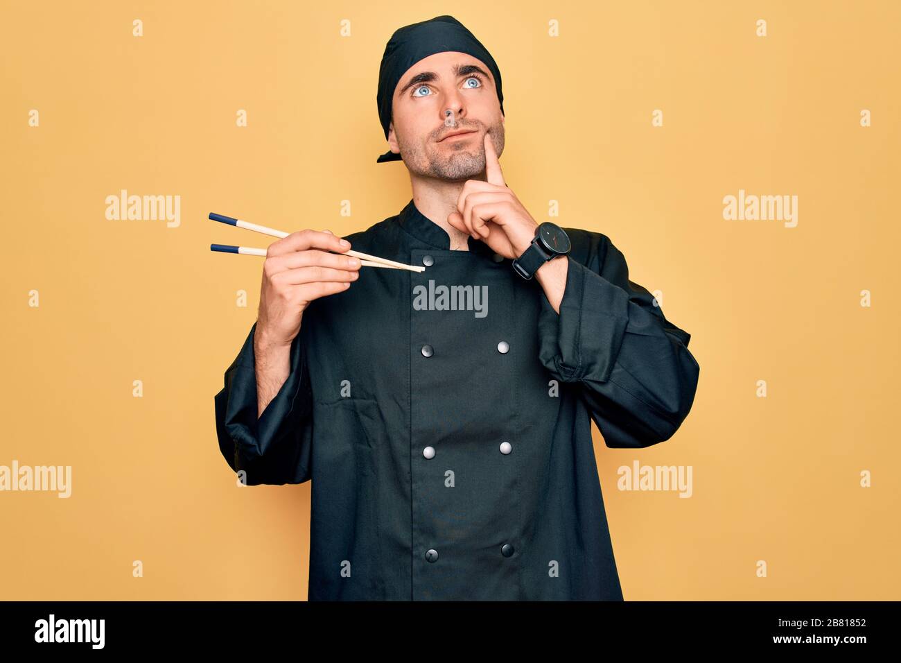 Young handsome cooker man with blue eyes wearing uniform and hat using ...