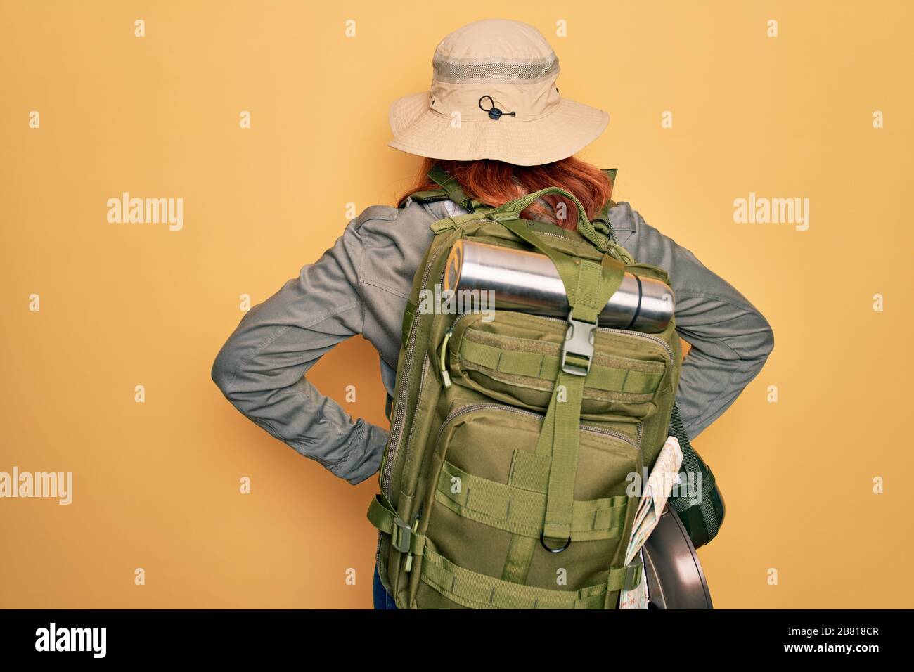 Young redhead backpacker woman hiking wearing backpack and hat over ...