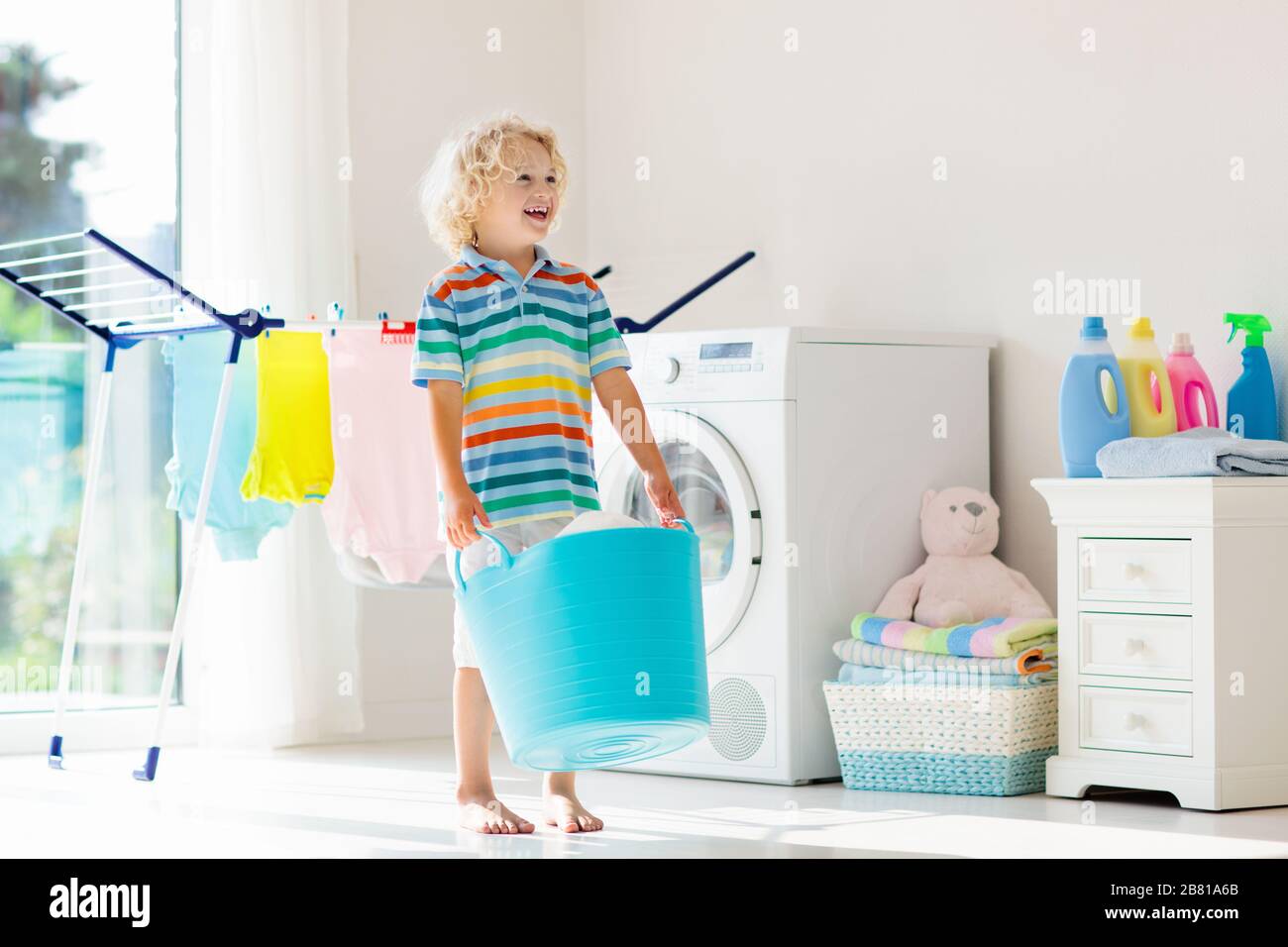 Child in laundry room with washing machine or tumble dryer. Kid helping ...