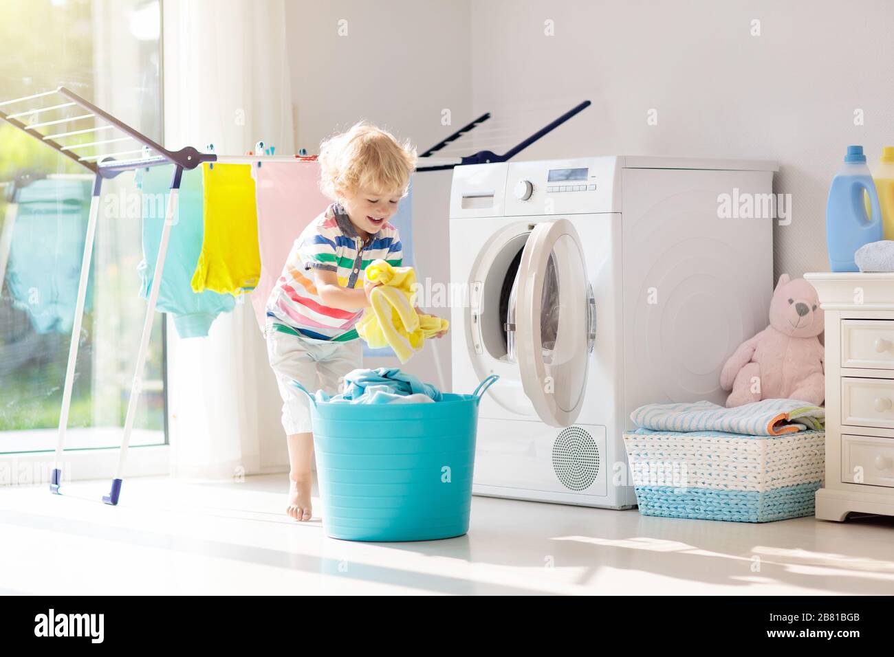 Child in laundry room with washing machine or tumble dryer. Kid helping ...