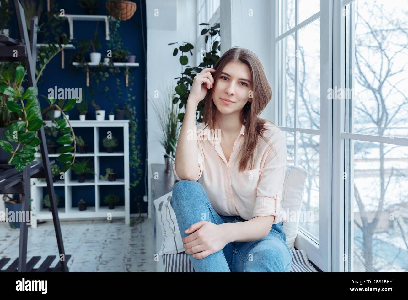 A brunette in blue jeans and a pink blouse smiles prettily and adjusts ...