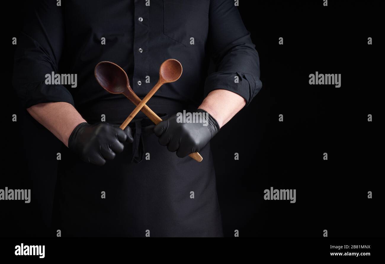 chef in black latex gloves and a black uniform holds crossed wooden ...