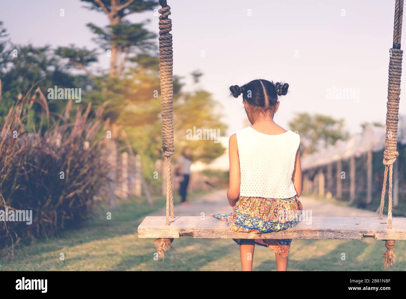 Back view of young girl sit on swings for wait her mom in the organic ...