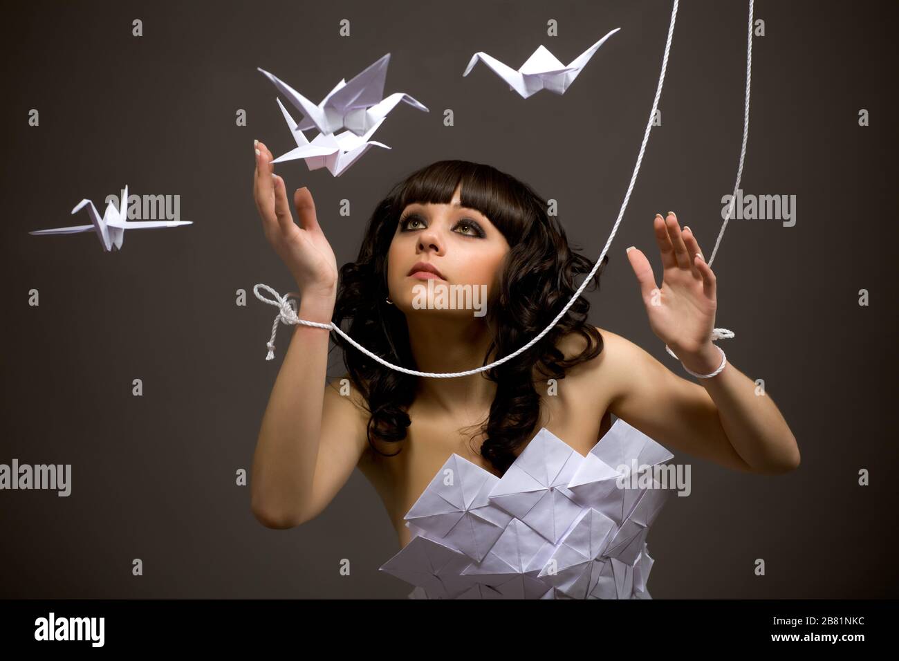 Portrait of a cute young sad girl in origami dress with moving arms ...