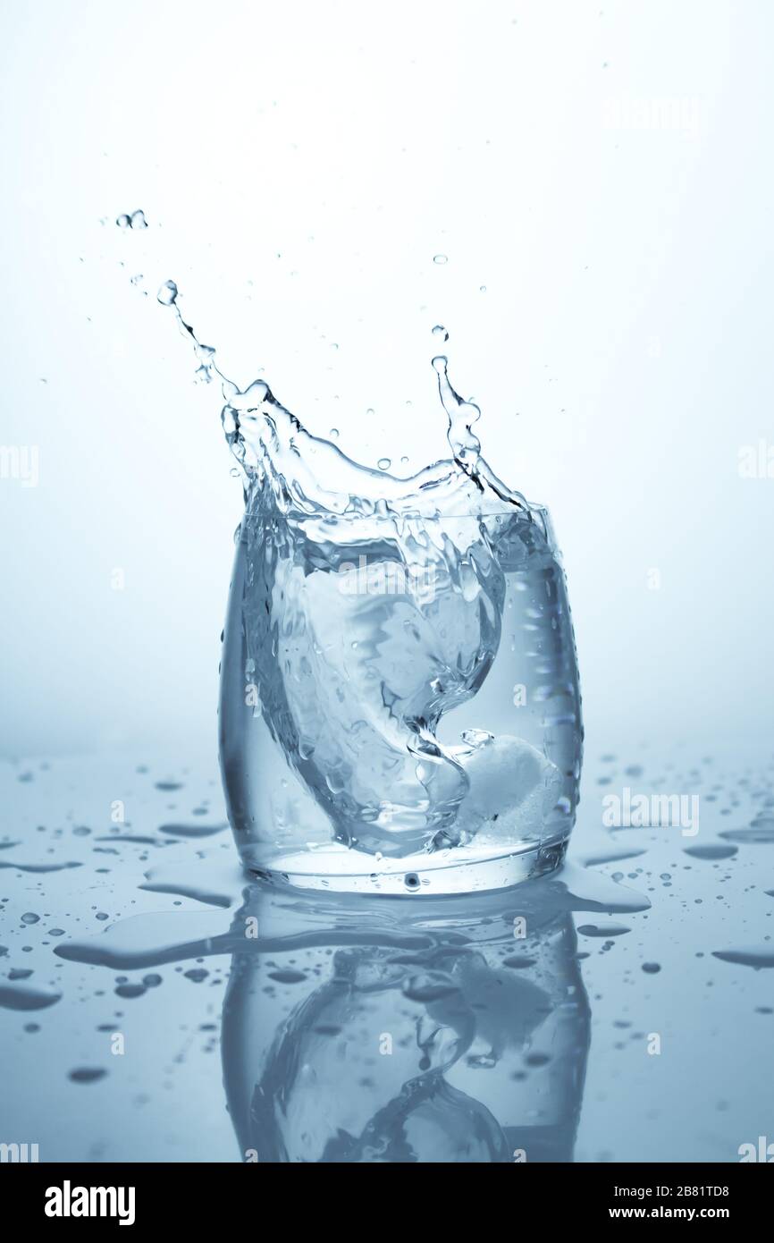 A piece of ice falling in a glass of water and raising a big splash ...