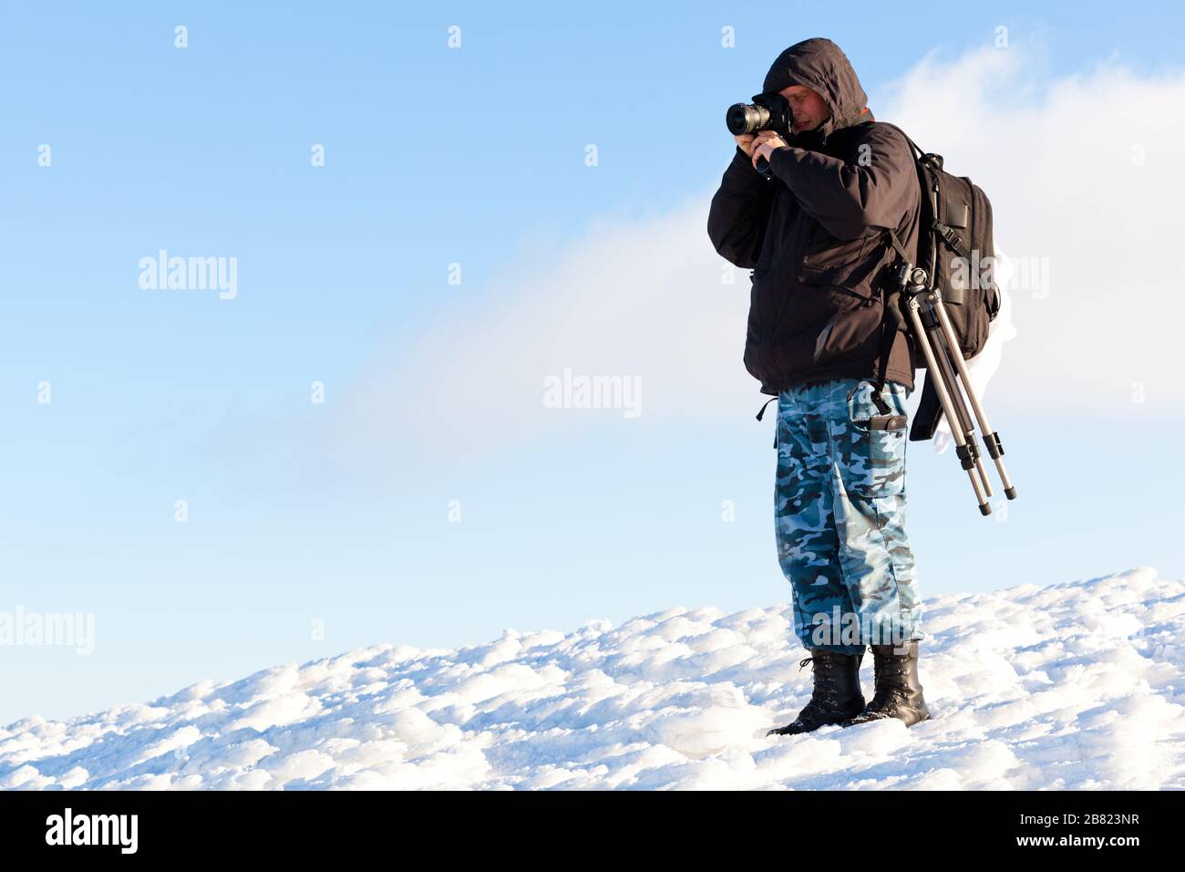 Young man photographer in winter clothing standing and making photo ...