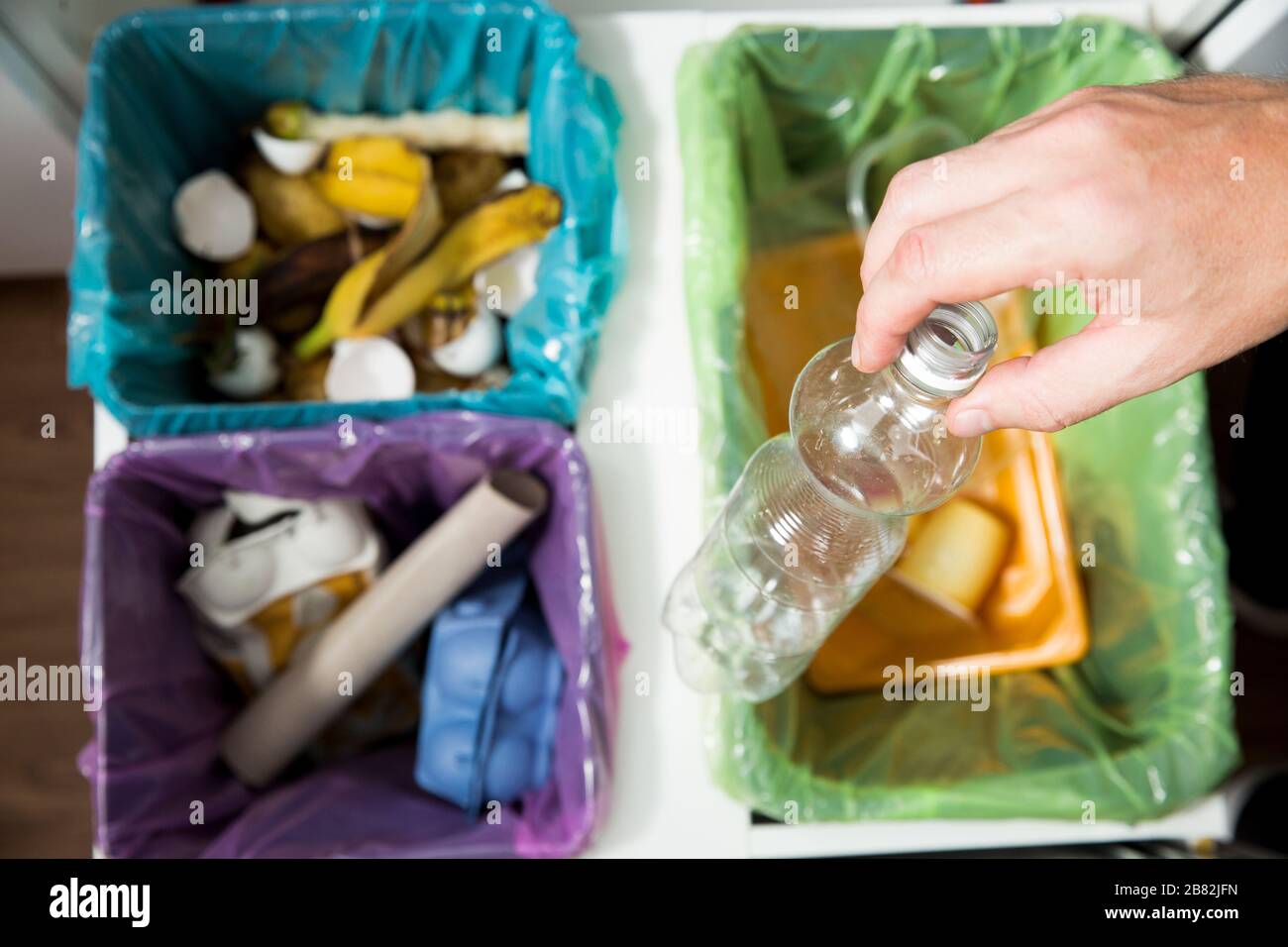 Man putting empty plastic bottle in recycling bin in the kitchen ...