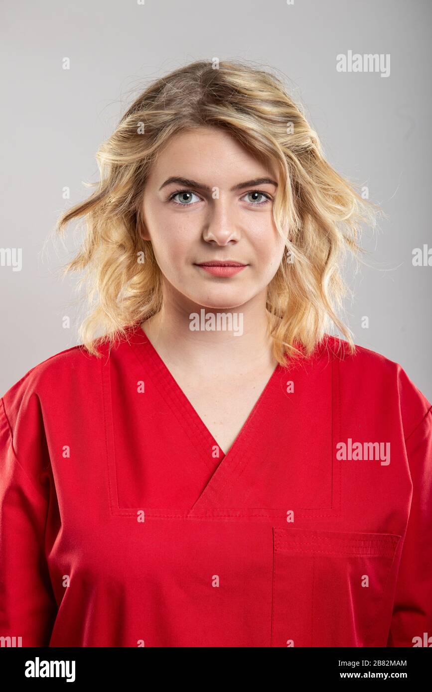 Portrait of female young nurse wearing red scrub on studio gray ...