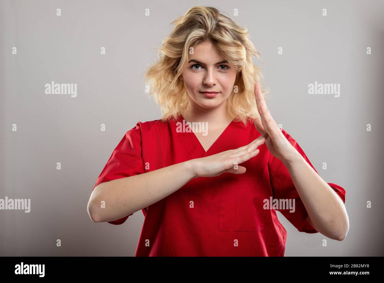 Portrait of female nurse wearing red scrub making time out gesture on ...