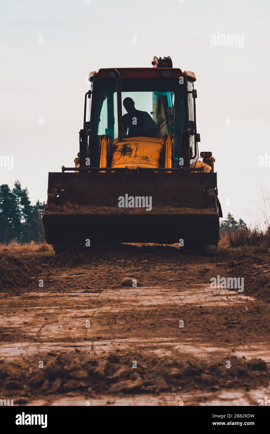 A close-up excavator loads soil into the bucket for further road ...