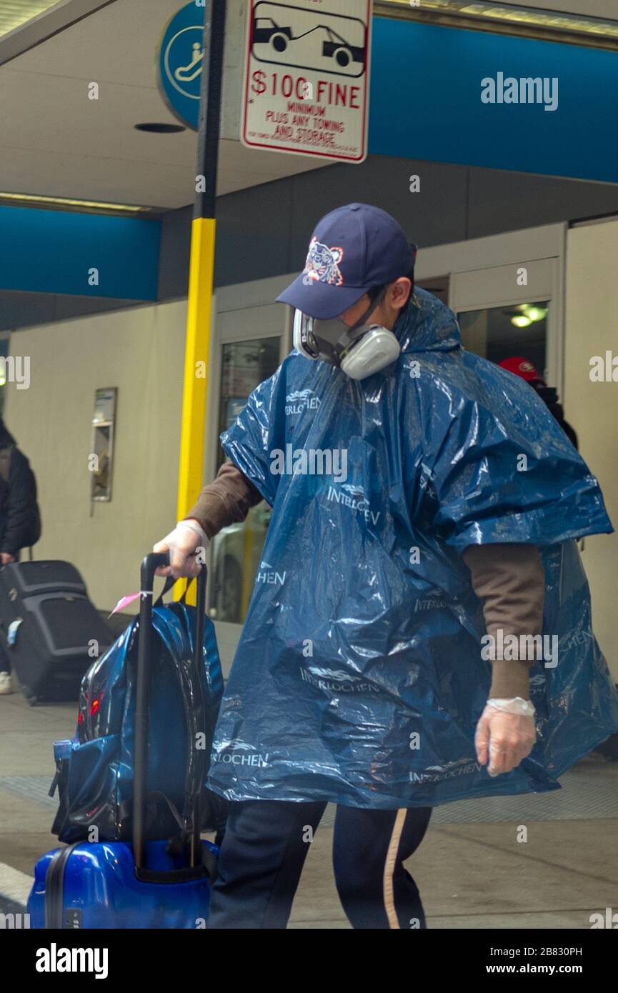 A traveler holding a suitcase and wearing gloves, a full respirator and ...