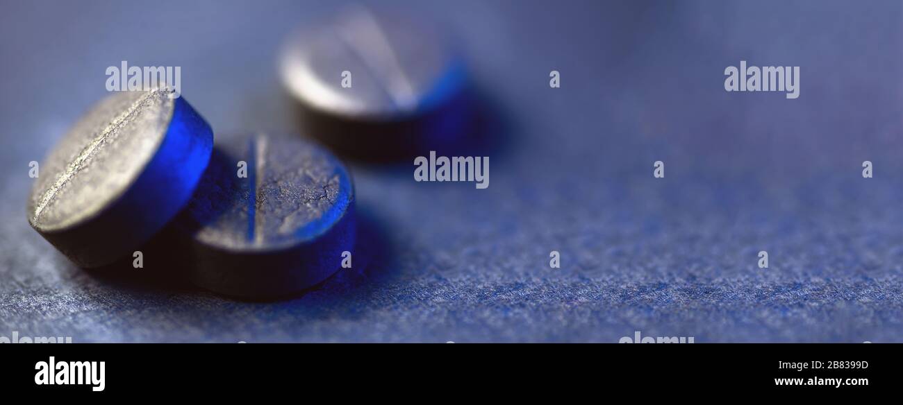 Three black activated charcoal tablets. On a black background. There's ...