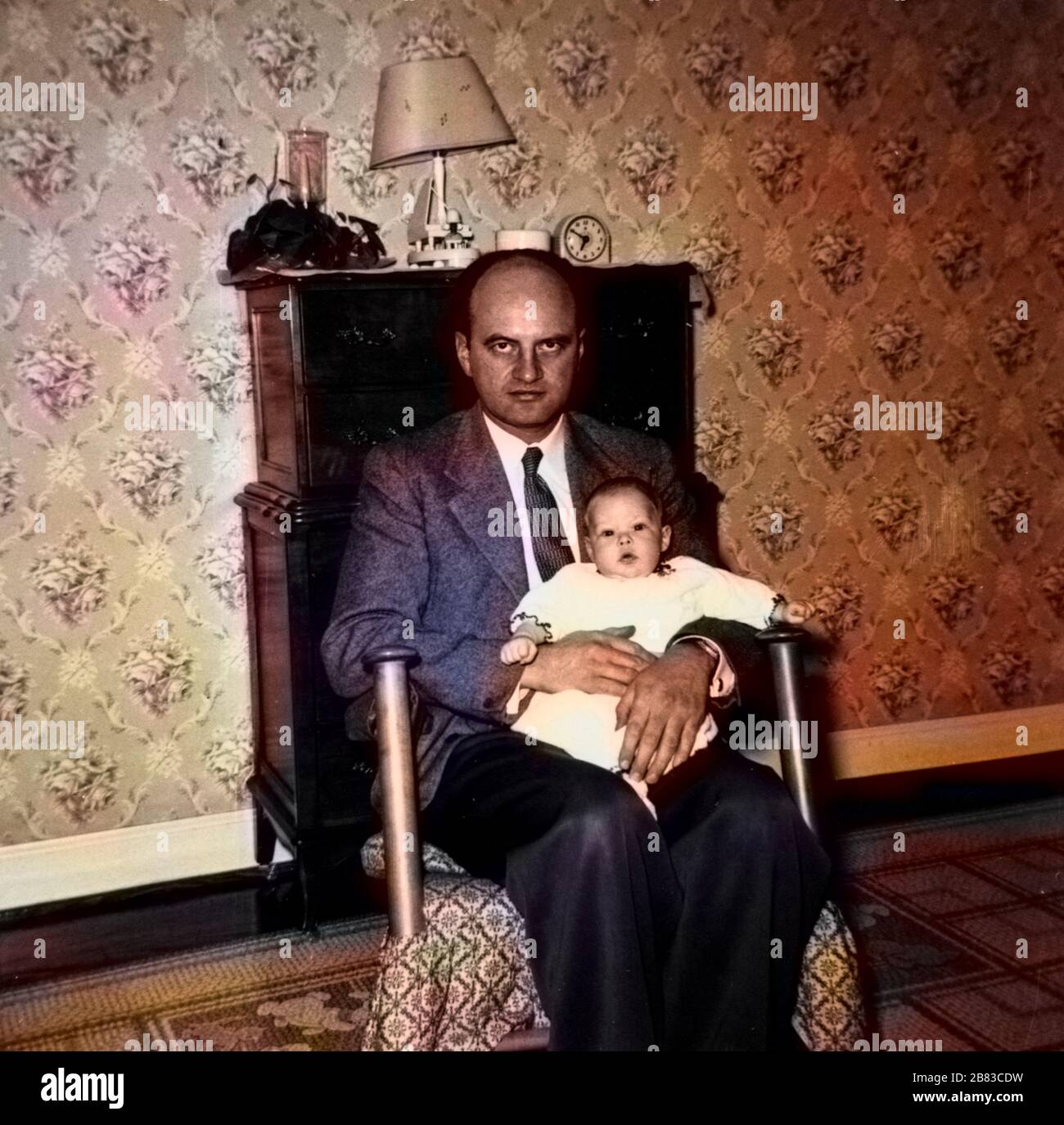 Formally dressed father, starkly lit, sitting in a rocking chair in a ...