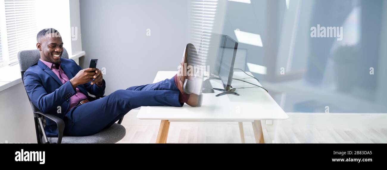 Lazy Man Using Phone At Work Desk Instead Of Working Stock Photo - Alamy