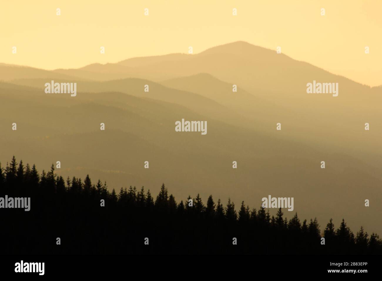Warm gradient of dawn sky above layers of mountain and rock silhouettes ...