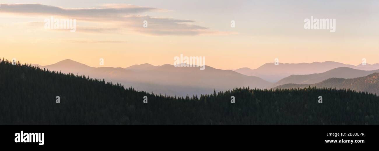 Warm gradient of dawn sky above layers of mountain and rock silhouettes ...
