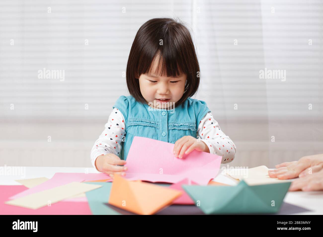 toddler girl learn making Origami at home against white background ...