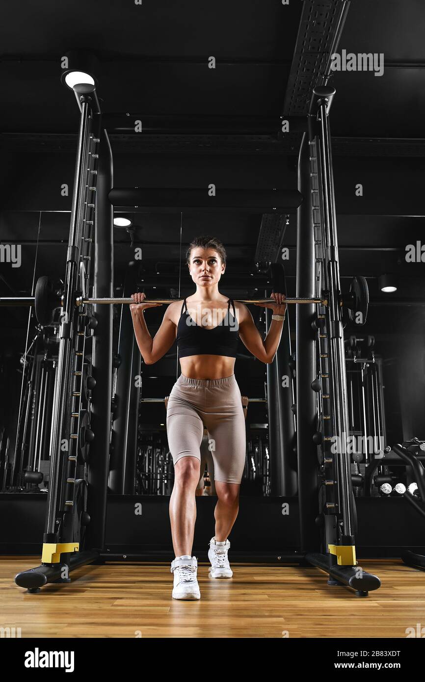 A girl is training her legs in the gym with a barbell. Sport lifestyle ...