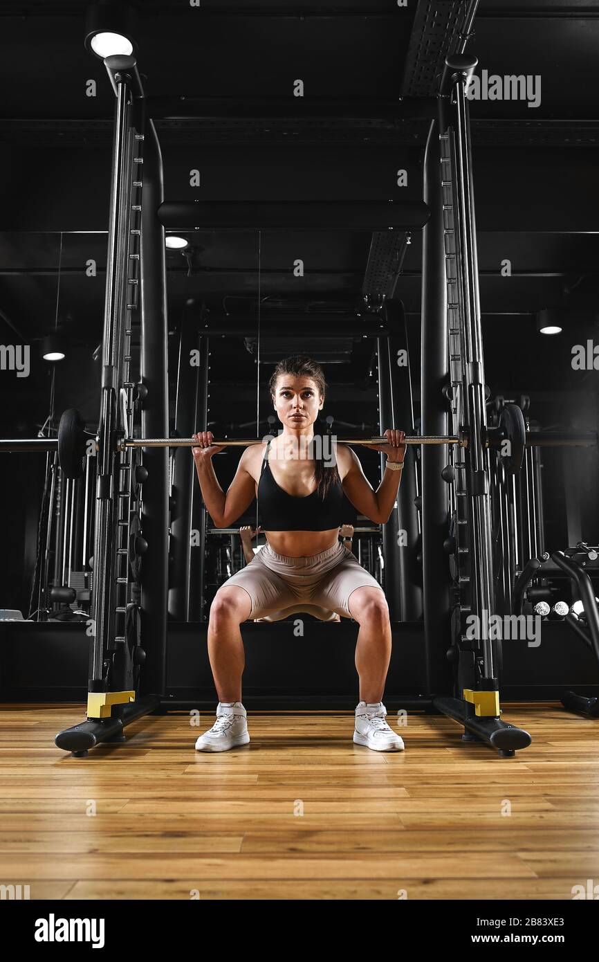 A girl is training her legs in the gym with a barbell. Sport lifestyle ...