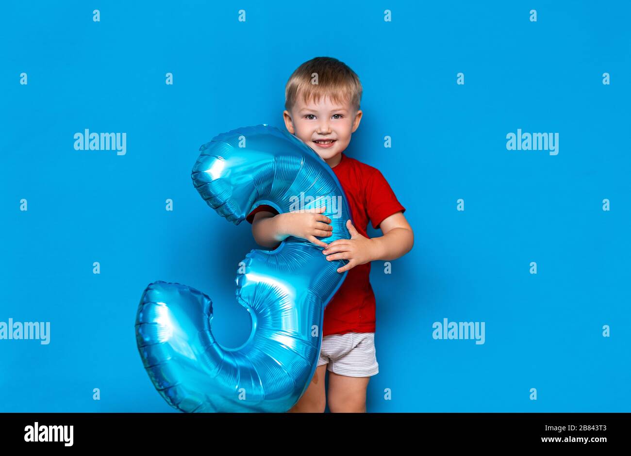 small cute blonde boy on blue background holding foil-coated sphere ...