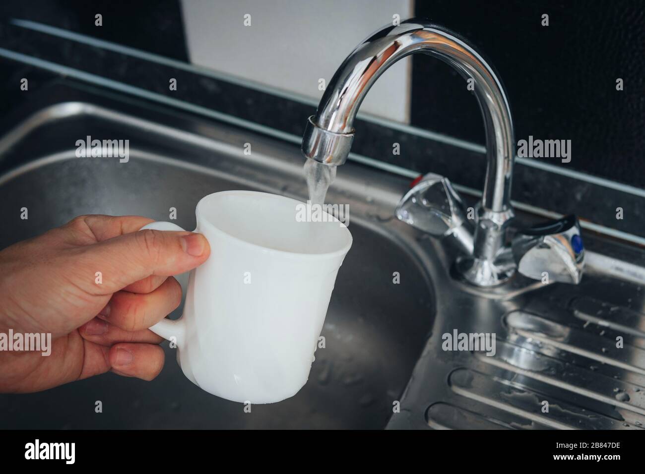 Modern faucet and sink in home kitchen. Man pouring fresh drink to cup ...