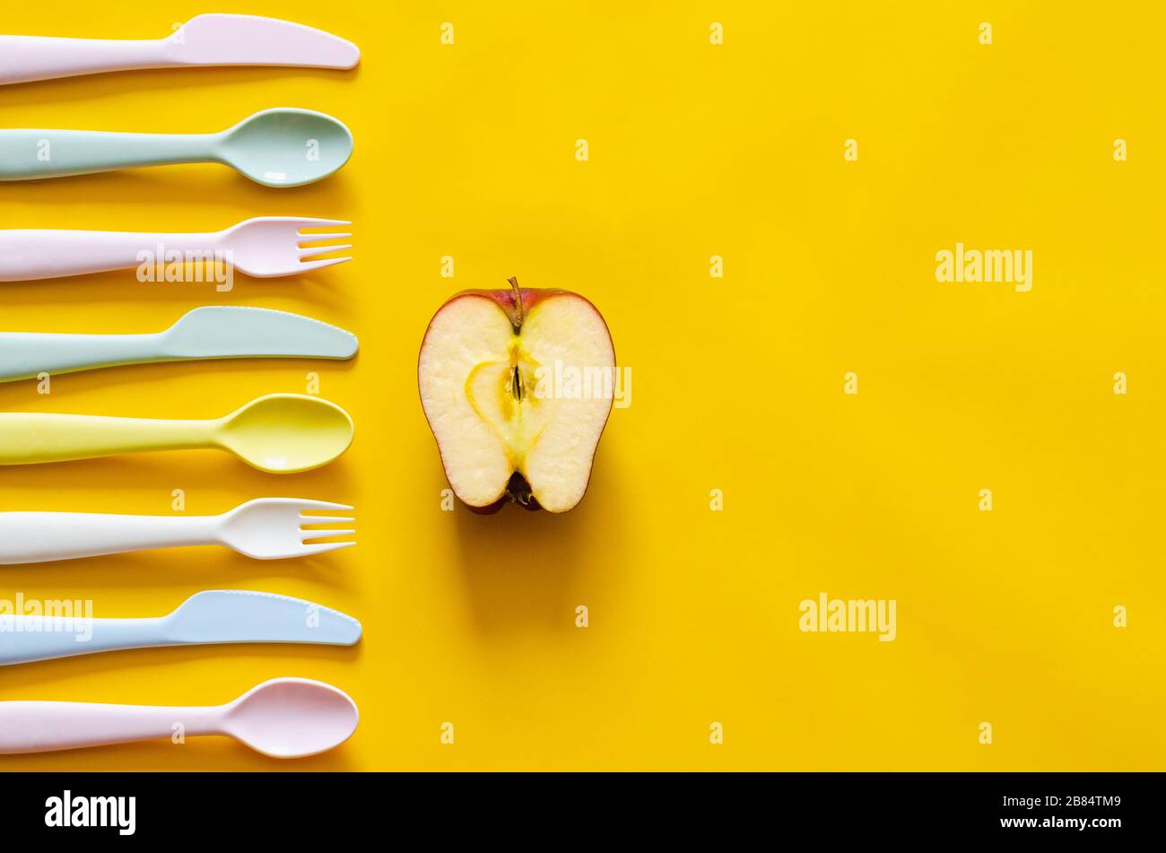 Colorful fork, spoon and knife with cutting apple on yellow background ...