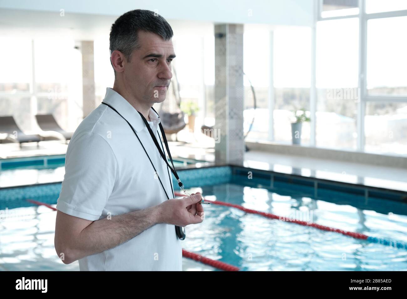 Serious mature swimming coach standing at pool and using stopwatch ...