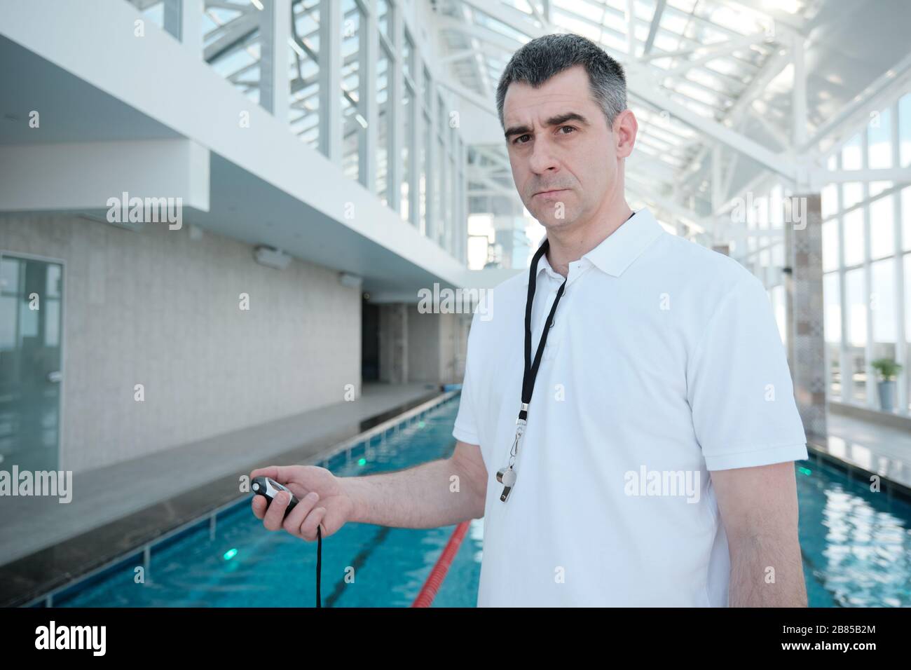 Portrait of serious strict mature coach with whistle using stopwatch ...