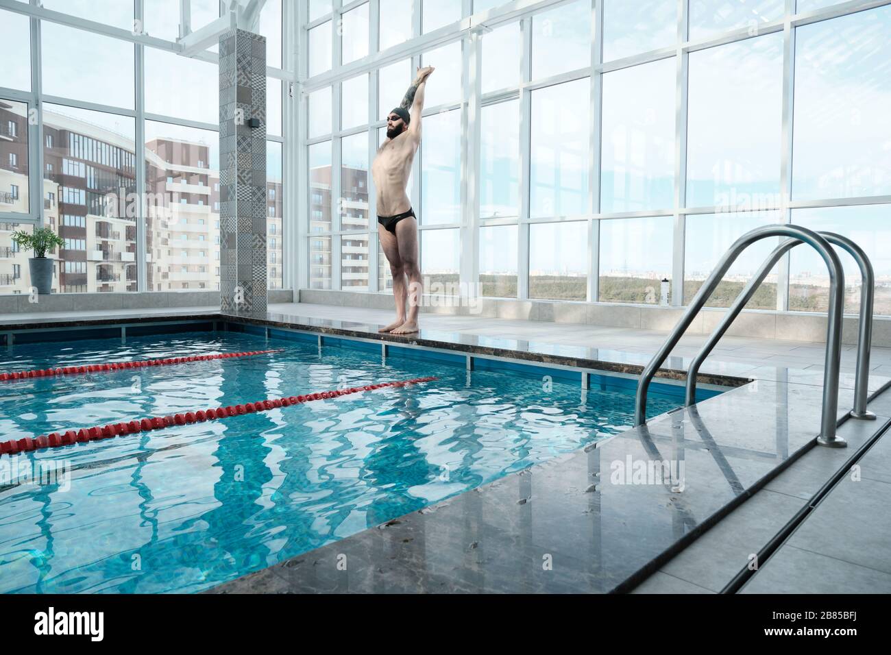 Bearded swimmer with muscular body standing on edge of pool and ...