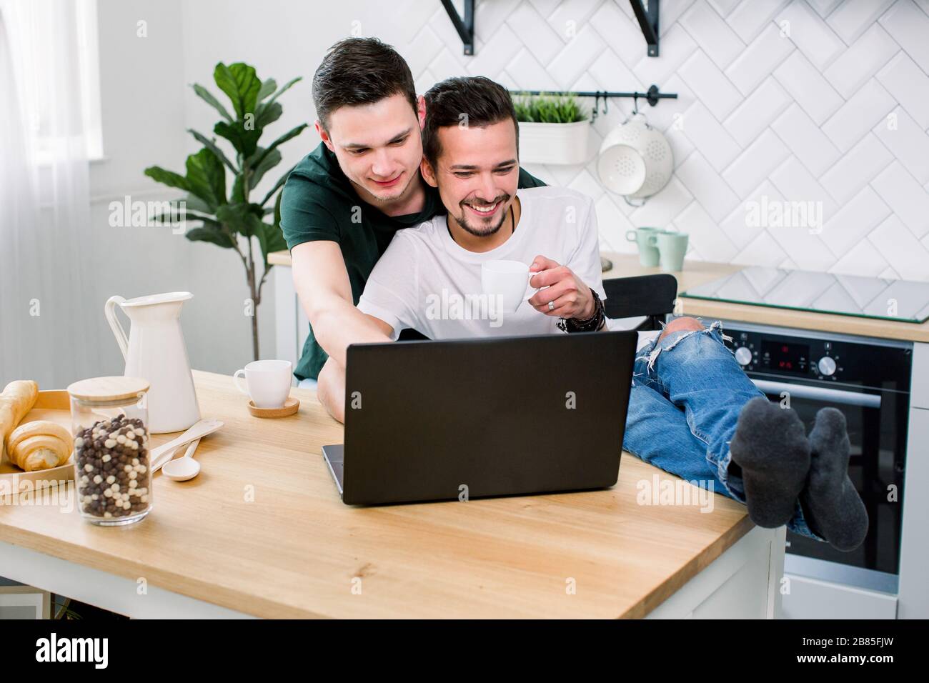 Happy gay male couple embracing while using laptop, having a good time ...