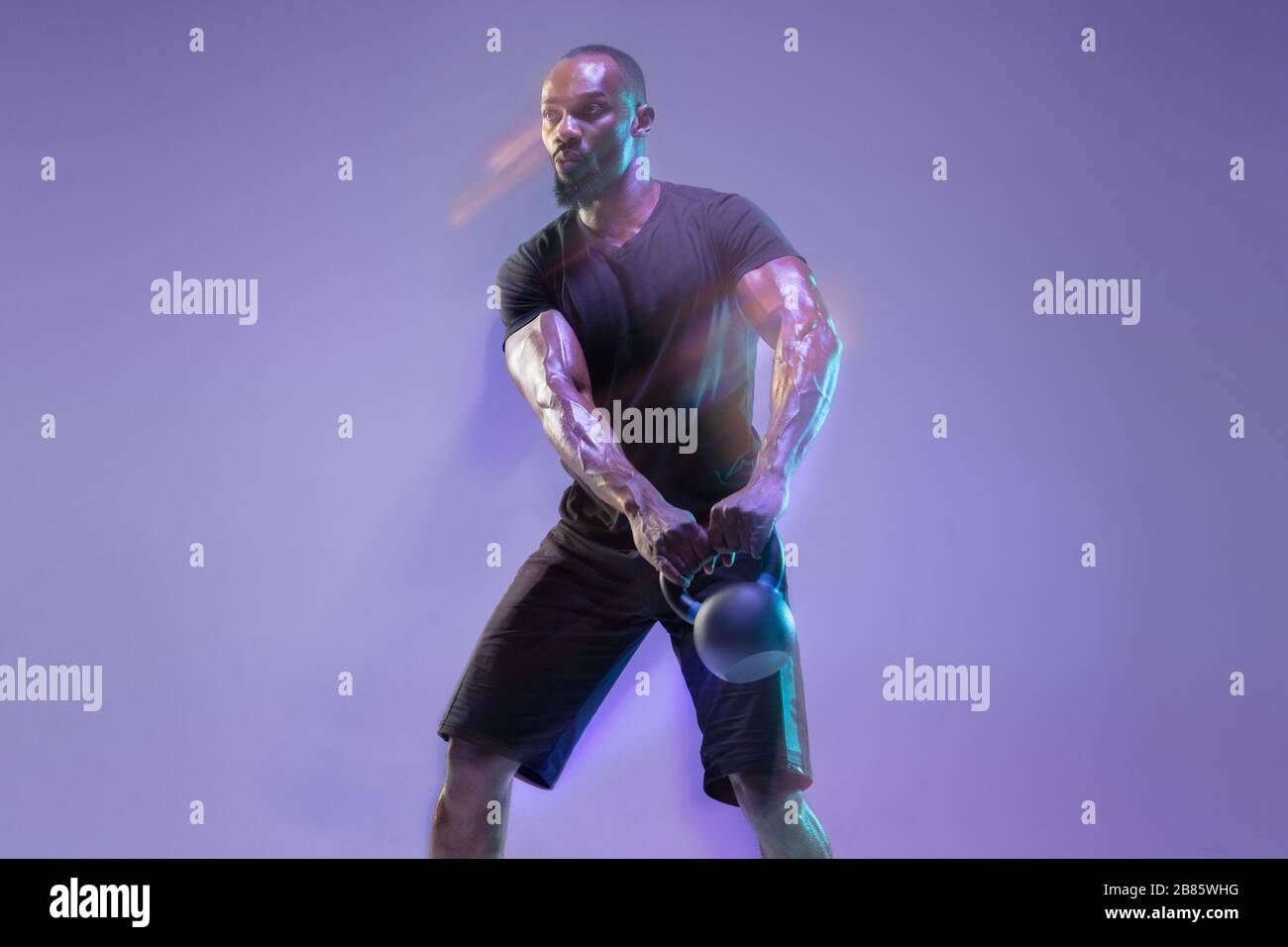 Move. Young african-american bodybuilder training over purple ...