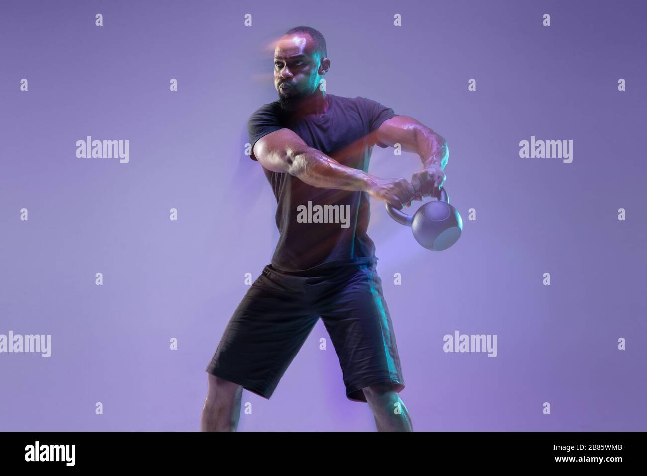 Move. Young african-american bodybuilder training over purple ...