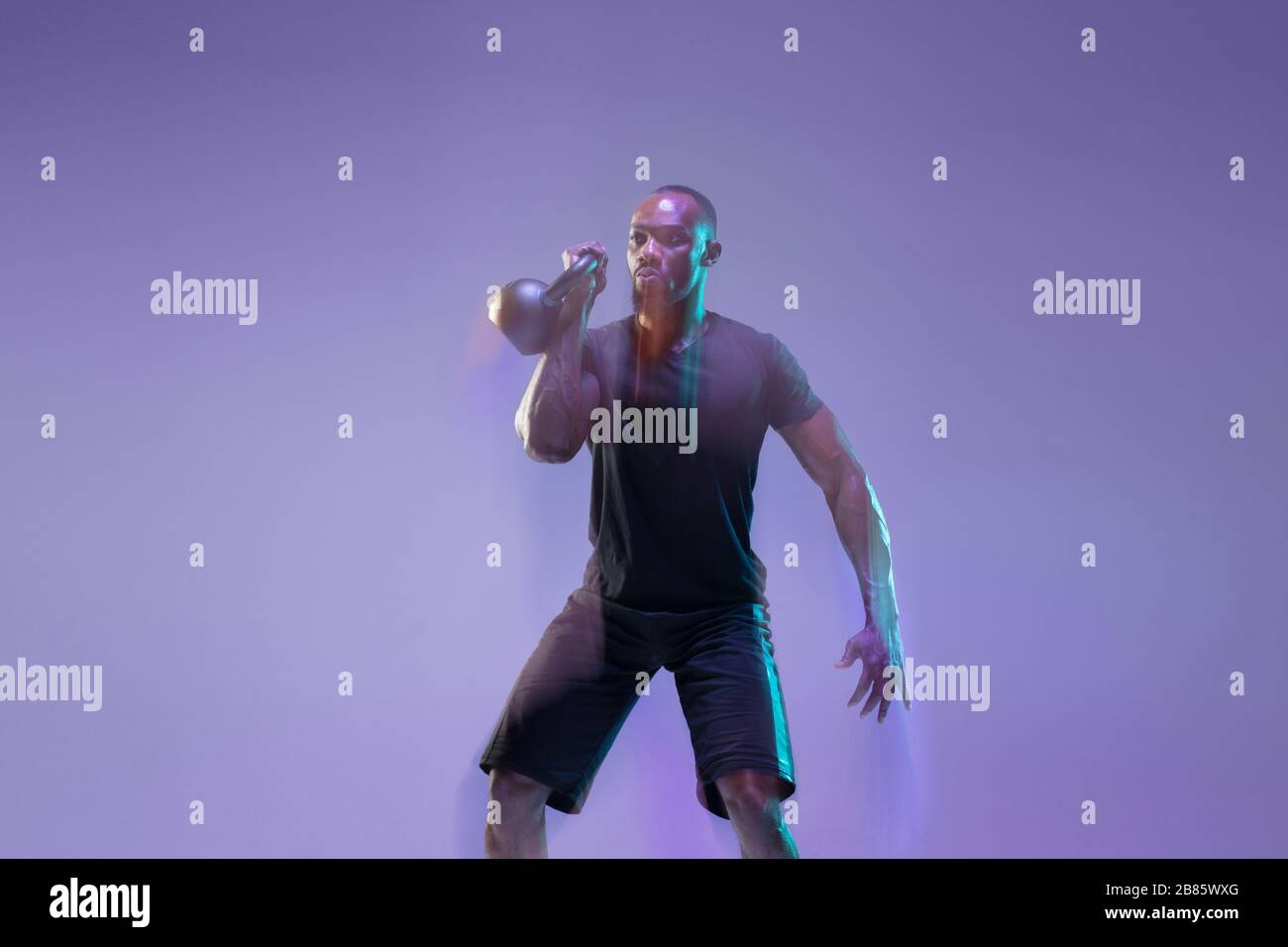 Move. Young african-american bodybuilder training over purple ...