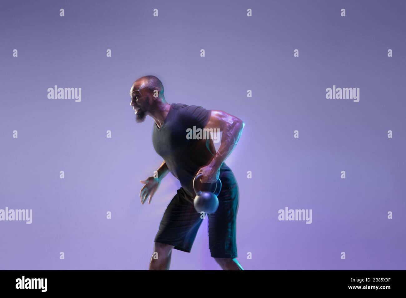 Emotions. Young african-american bodybuilder training over purple ...